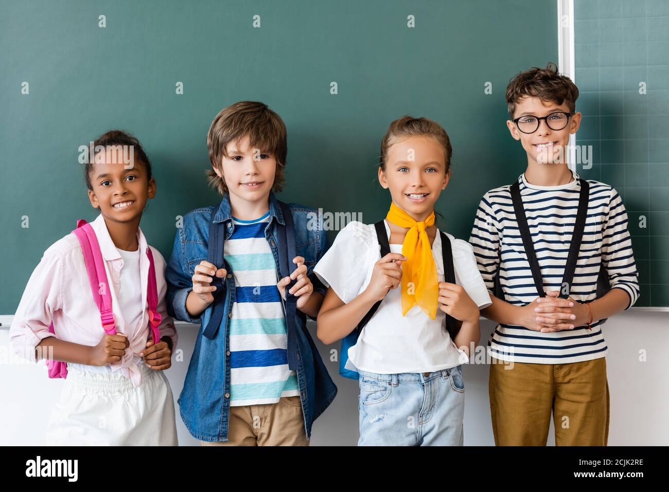 Multicultural schoolchildren with backpacks looking at camera near ...
