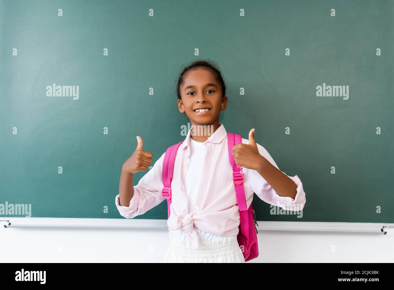African american schoolgirl showing thumbs up near chalkboard in ...