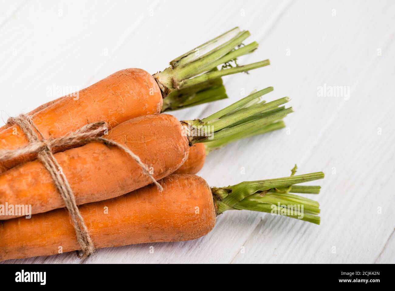 close up view of fresh carrots tied with rope on white wooden table ...