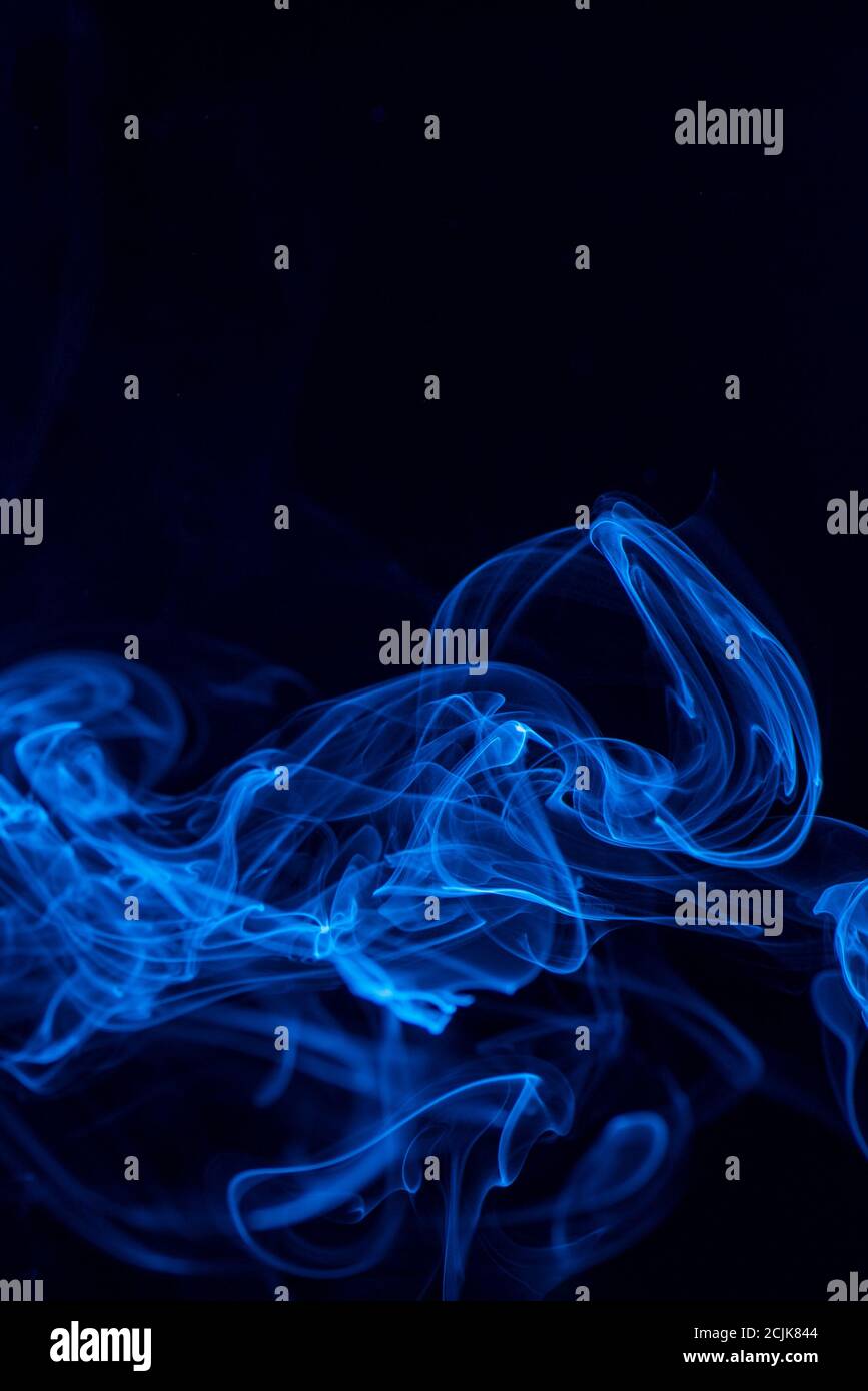 Conceptual image of blue color smoke isolated on dark black background ...