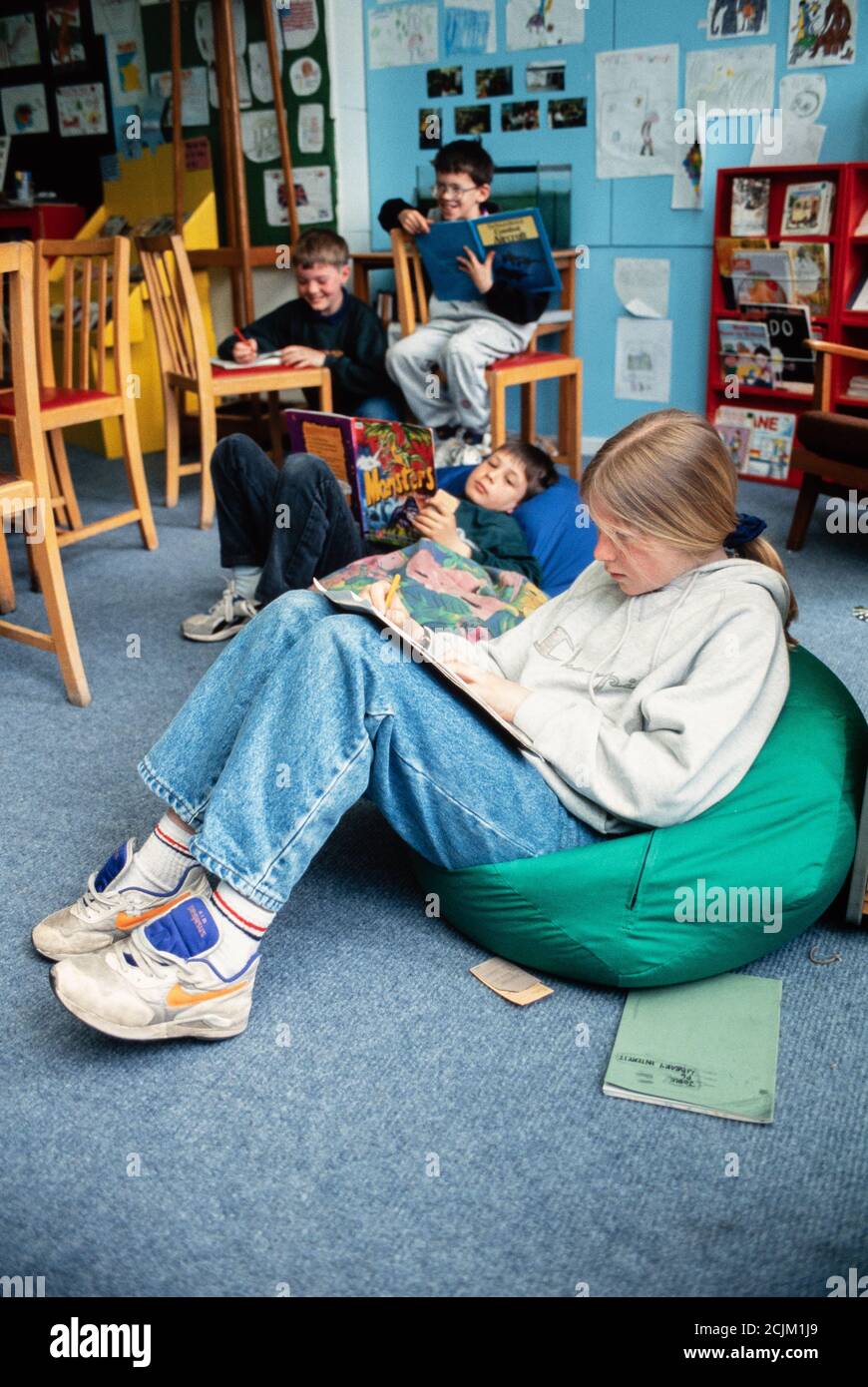 A girl sits on a beanbag chair writing in an exercise book whilst ...