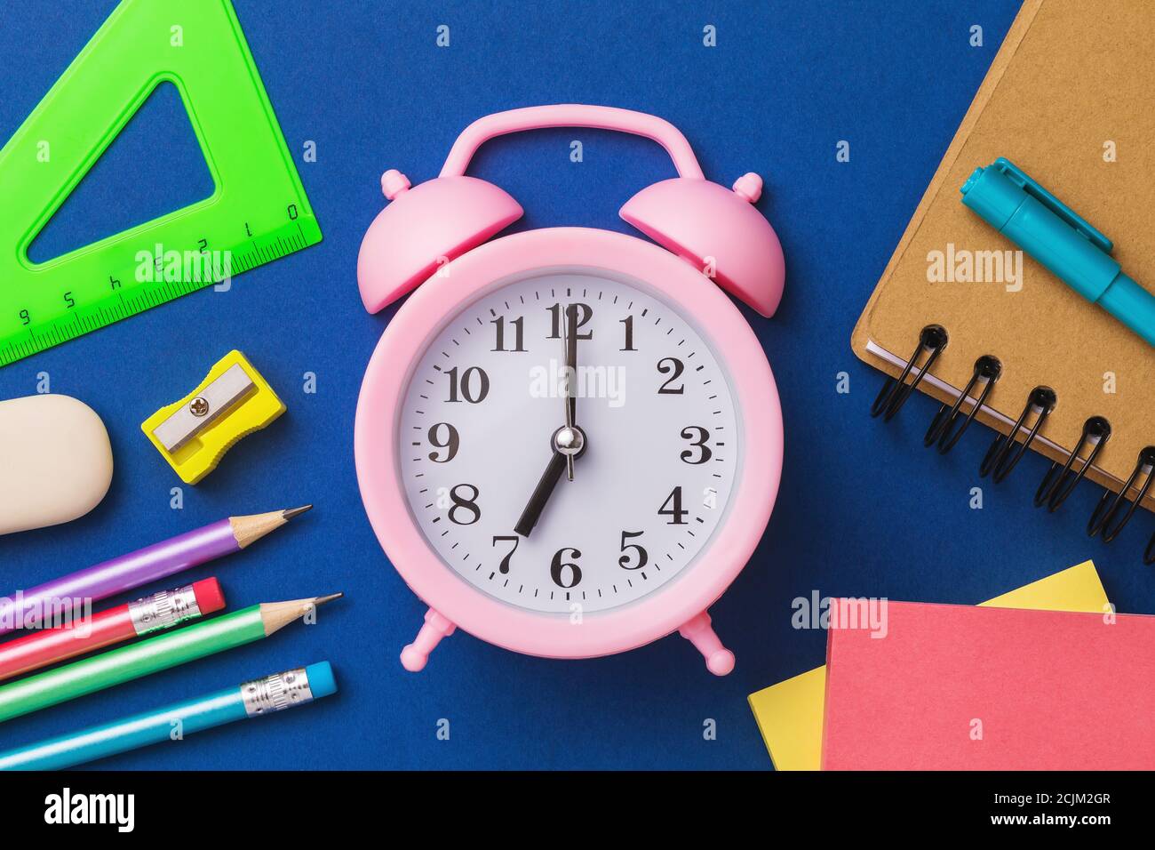 Alarm clock and school supplies on a blue background. The concept is ...