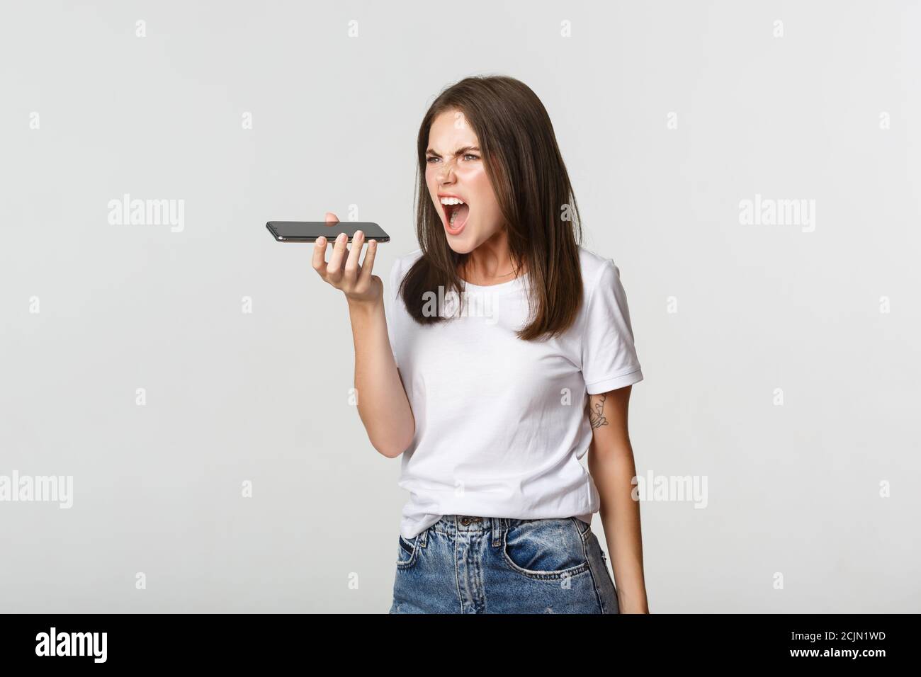 Angry brunette girl shouting mad while recording voice message, being ...