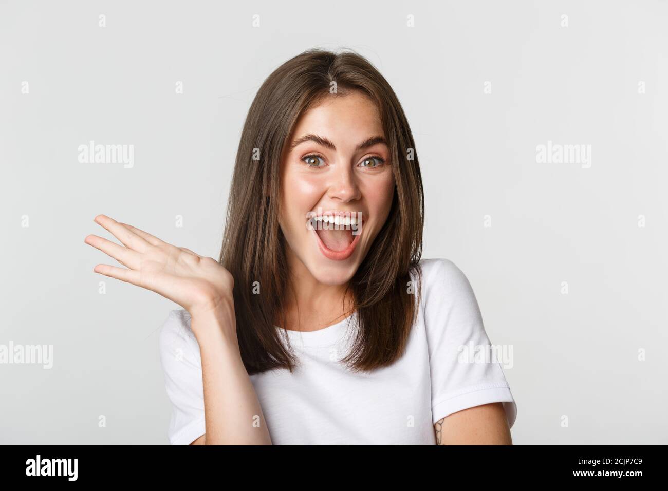 Close-up of excited beautiful brunette girl looking amused, waving hand ...