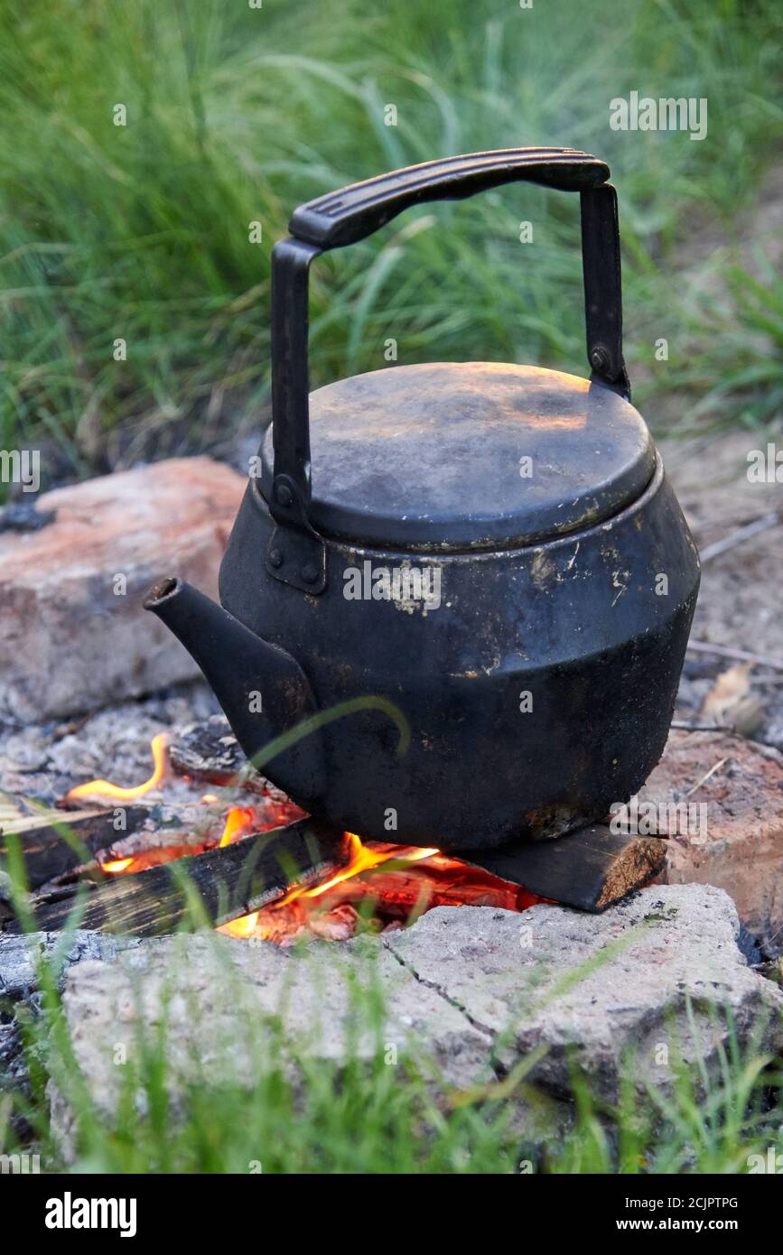 An old kettle stands on a fire in nature, preparing tea on a camping ...