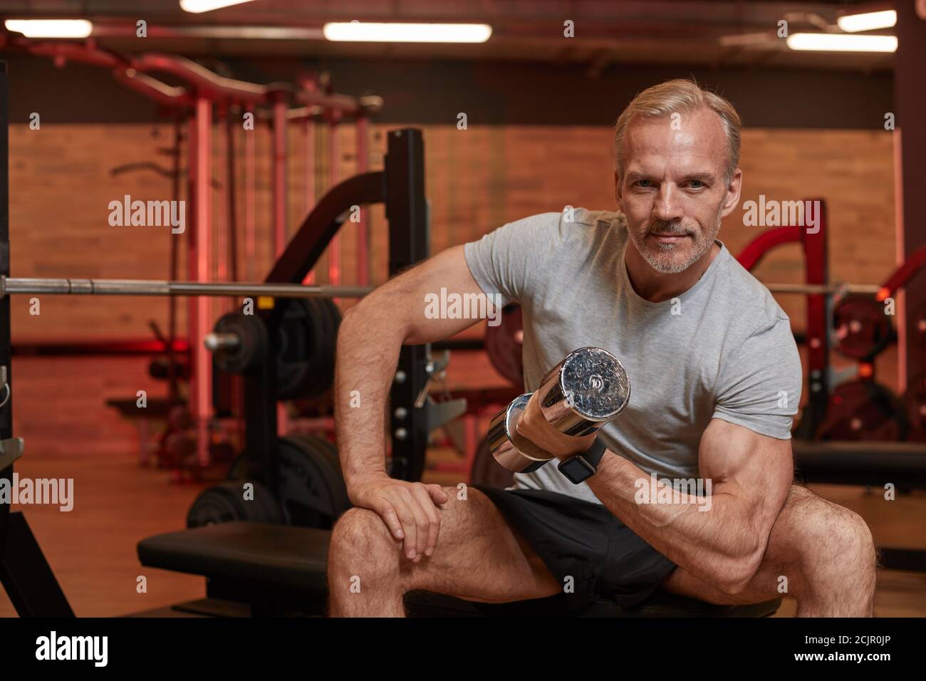 Portrait of mature muscle man lifting barbell and doing physical ...