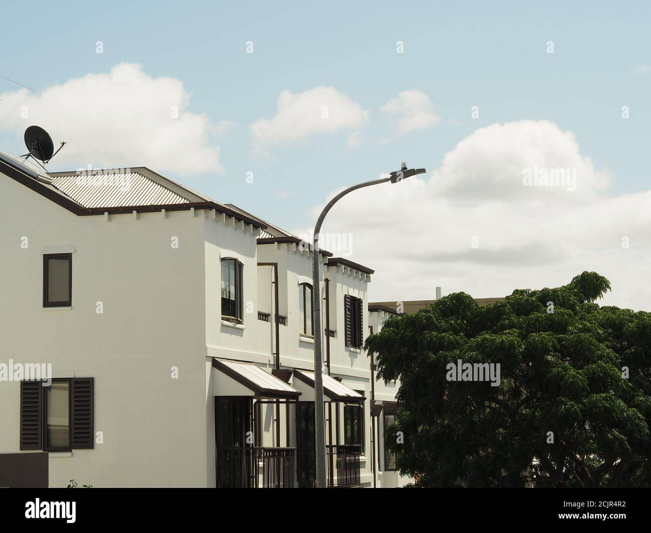 White-colored modern rural house with balconies, next to green trees ...