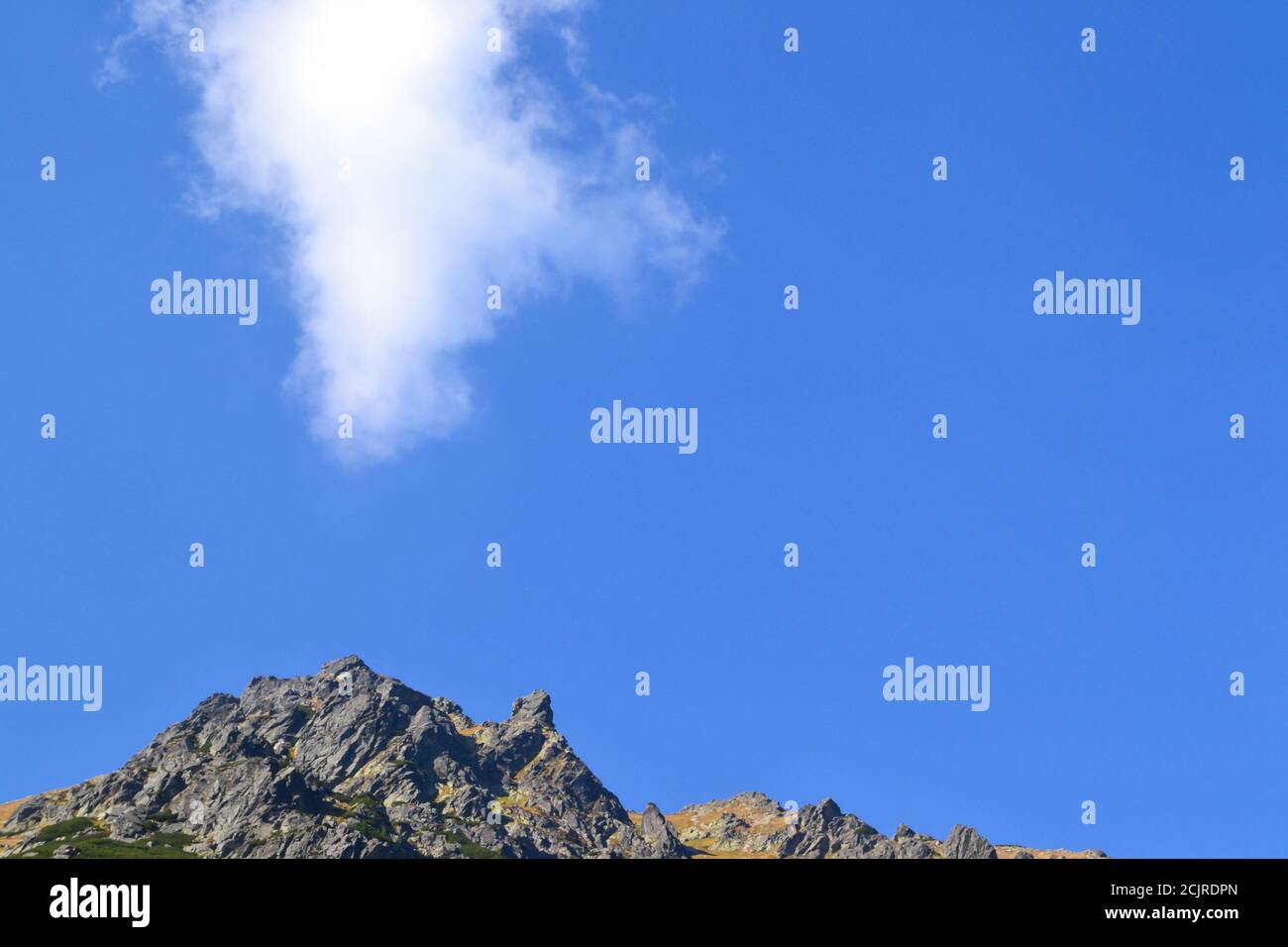 A cloud against a blue sky hovered over the top of the mountain ...