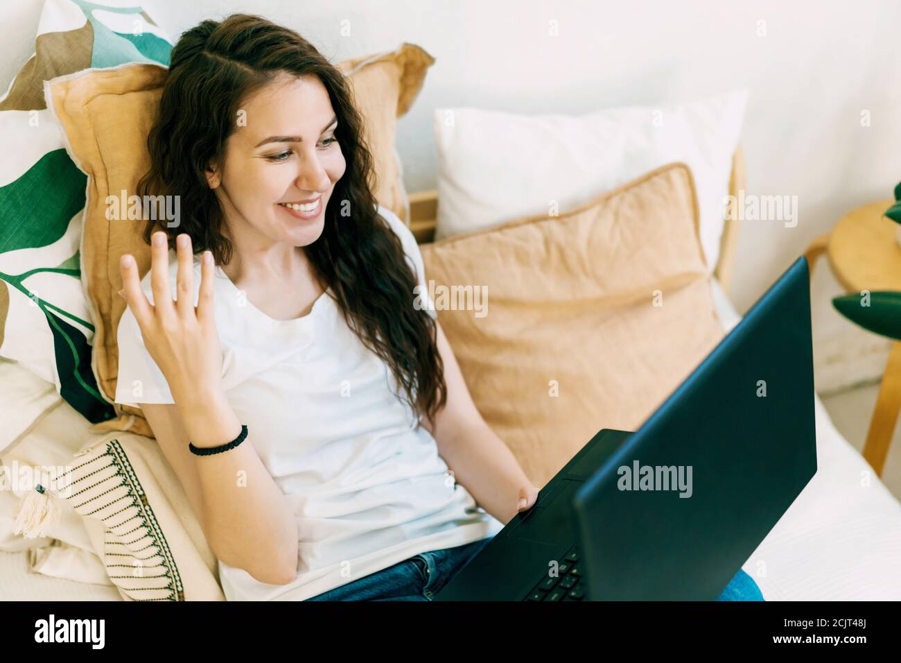 Young curly charming woman on the bed looks at the laptop and talks ...