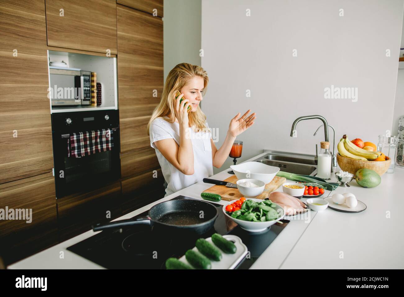 Young woman using mobile phone while cooking the meal in the kitchen ...