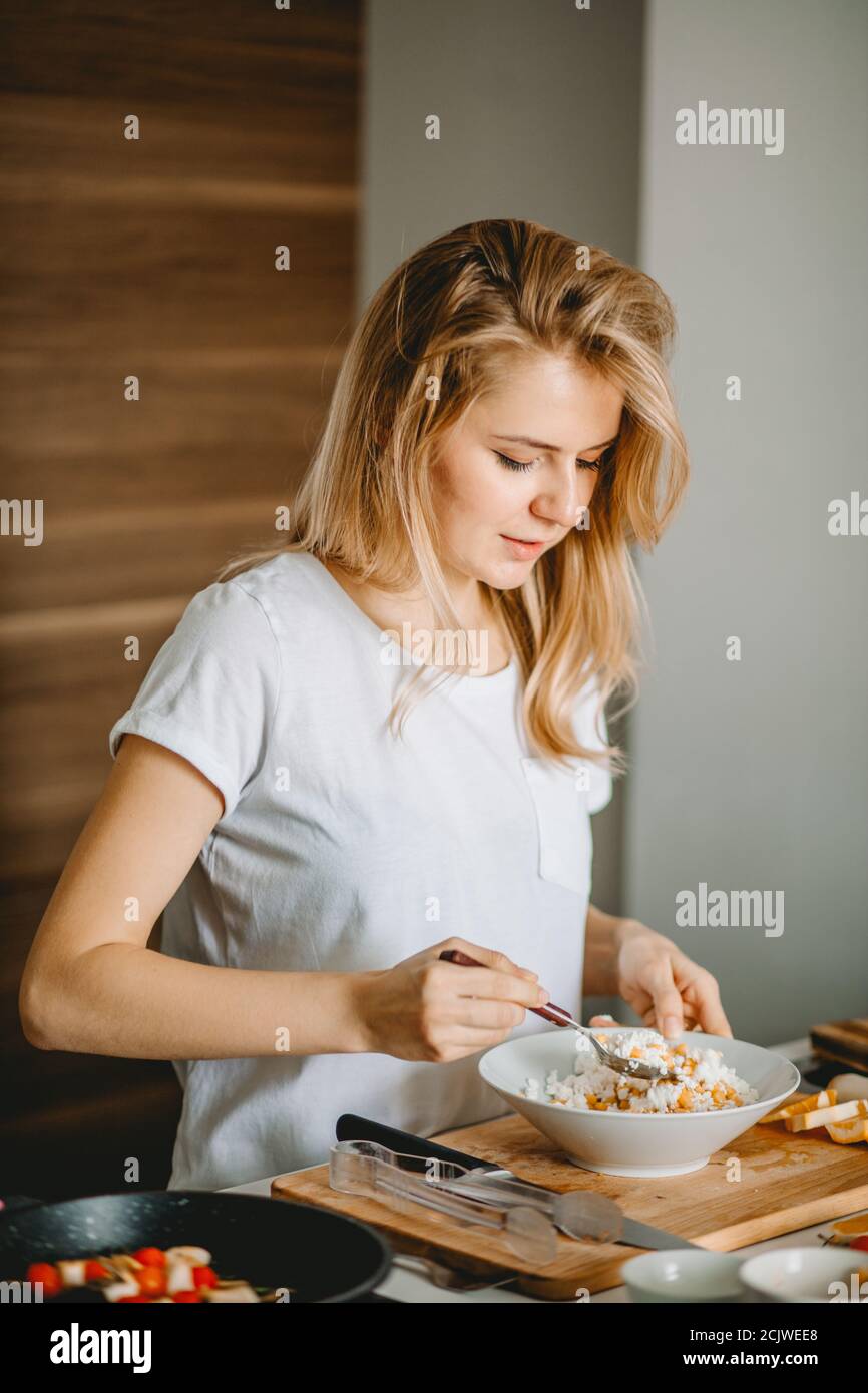 close up side view photo of blond woman cooking salad from rice and ...