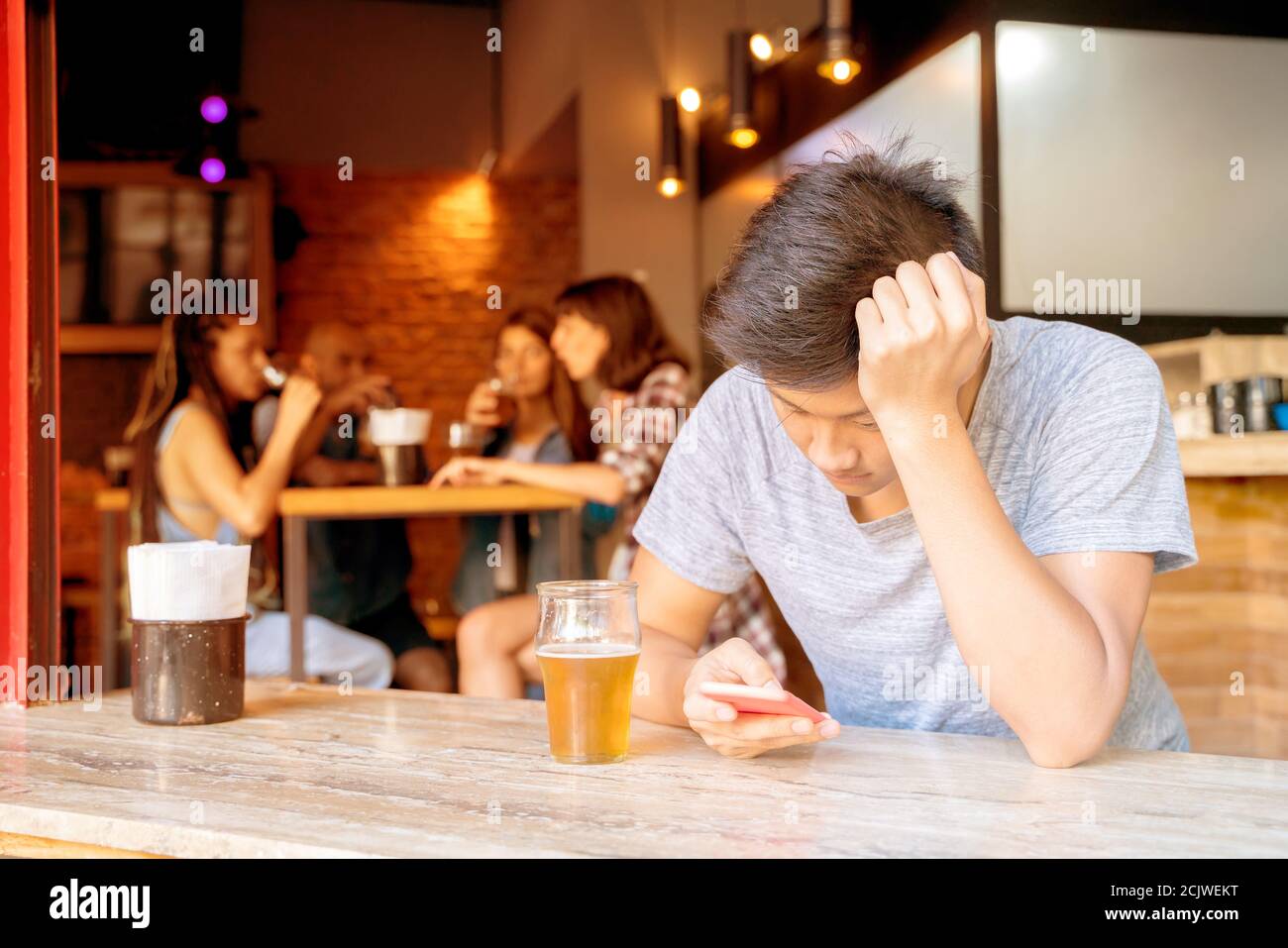 A sad handsome excluded asian boy sitting alone in a bar using his ...