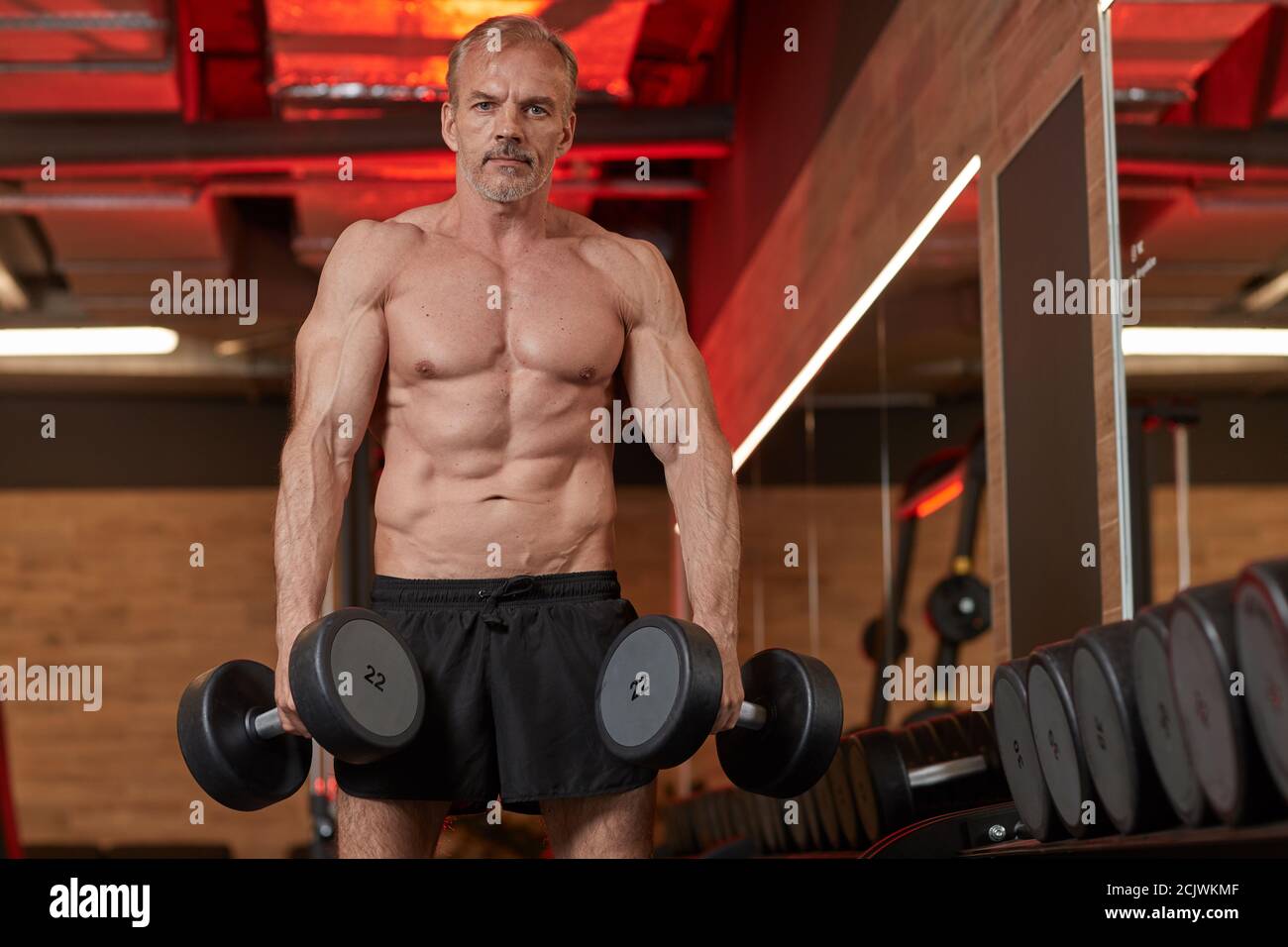 Portrait of shirtless muscle man lifting barbells and looking at camera ...