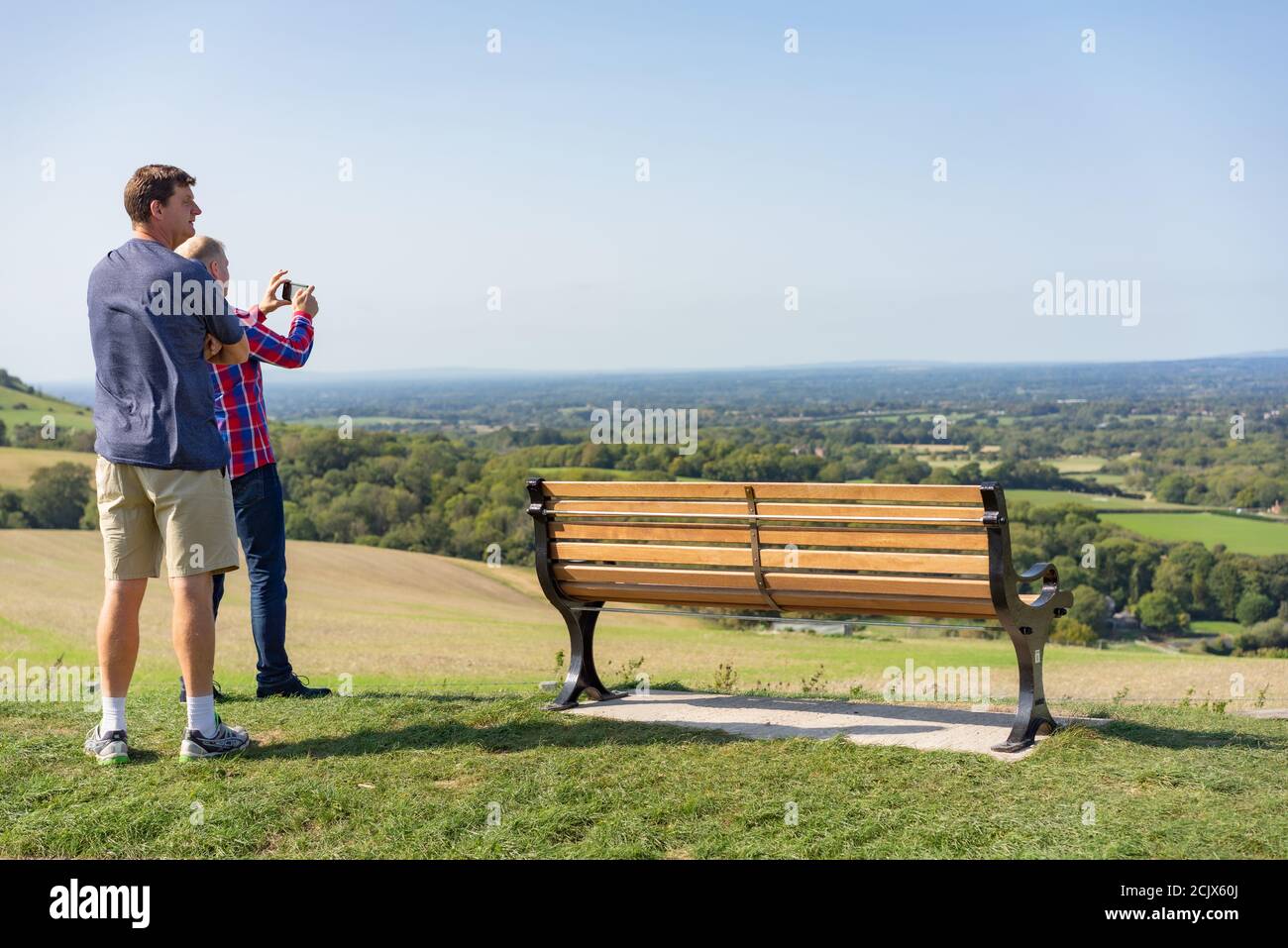 Two middle aged men stand beside a bench on the South Downs in southern ...