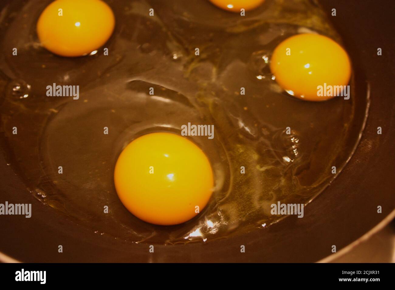 four chicken eggs being cooked in a round black pan Stock Photo - Alamy