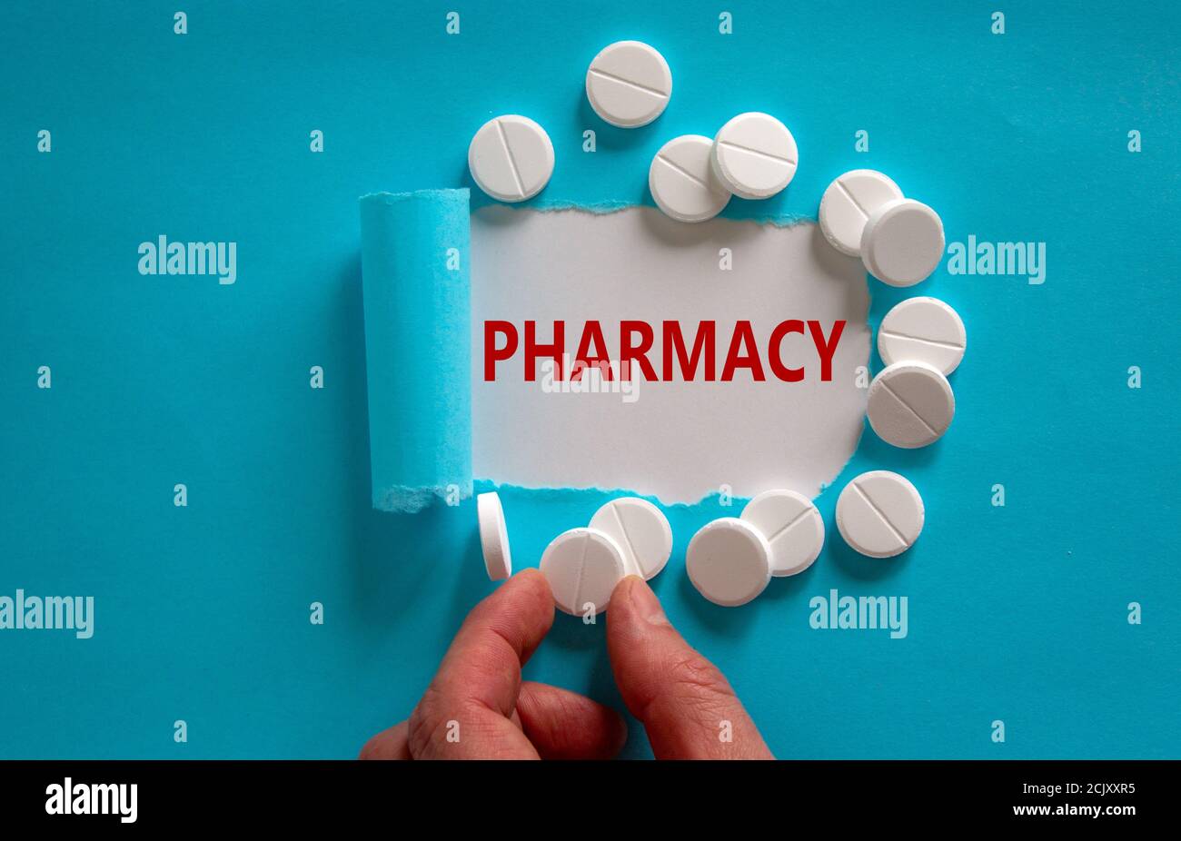 The word 'pharmacy' appearing behind torn blue paper. White pills and ...