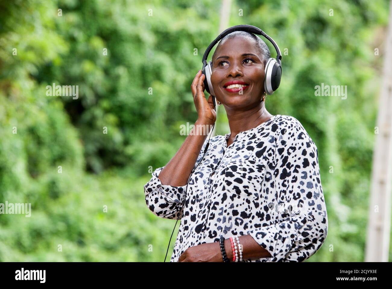 Cheerful woman listens to music using headphones in the park on green ...