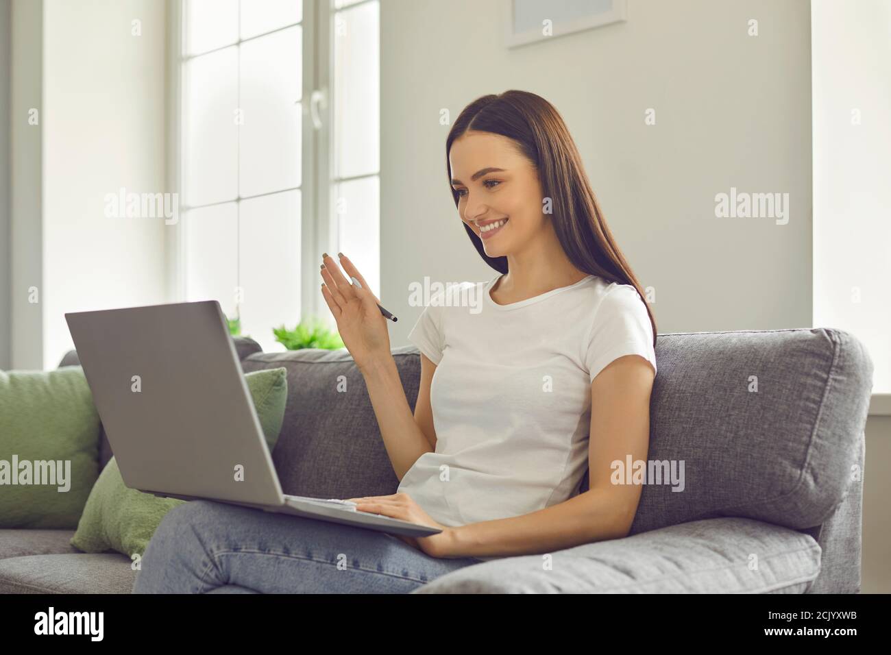 Smiling young teacher waving hand at laptop screen greeting her student ...