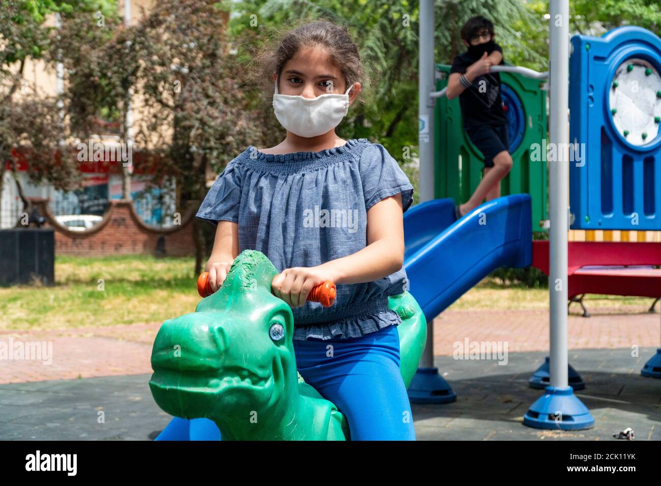 A preschool girl with a protective face mask is sitting on a spring ...