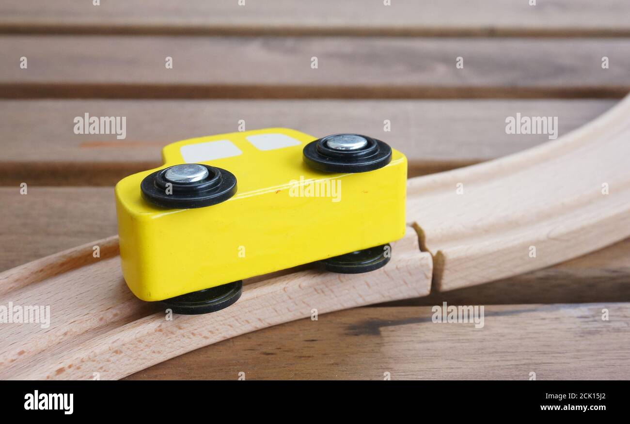 Closeup of a yellow wooden toy car lying on its side on a wooden track ...