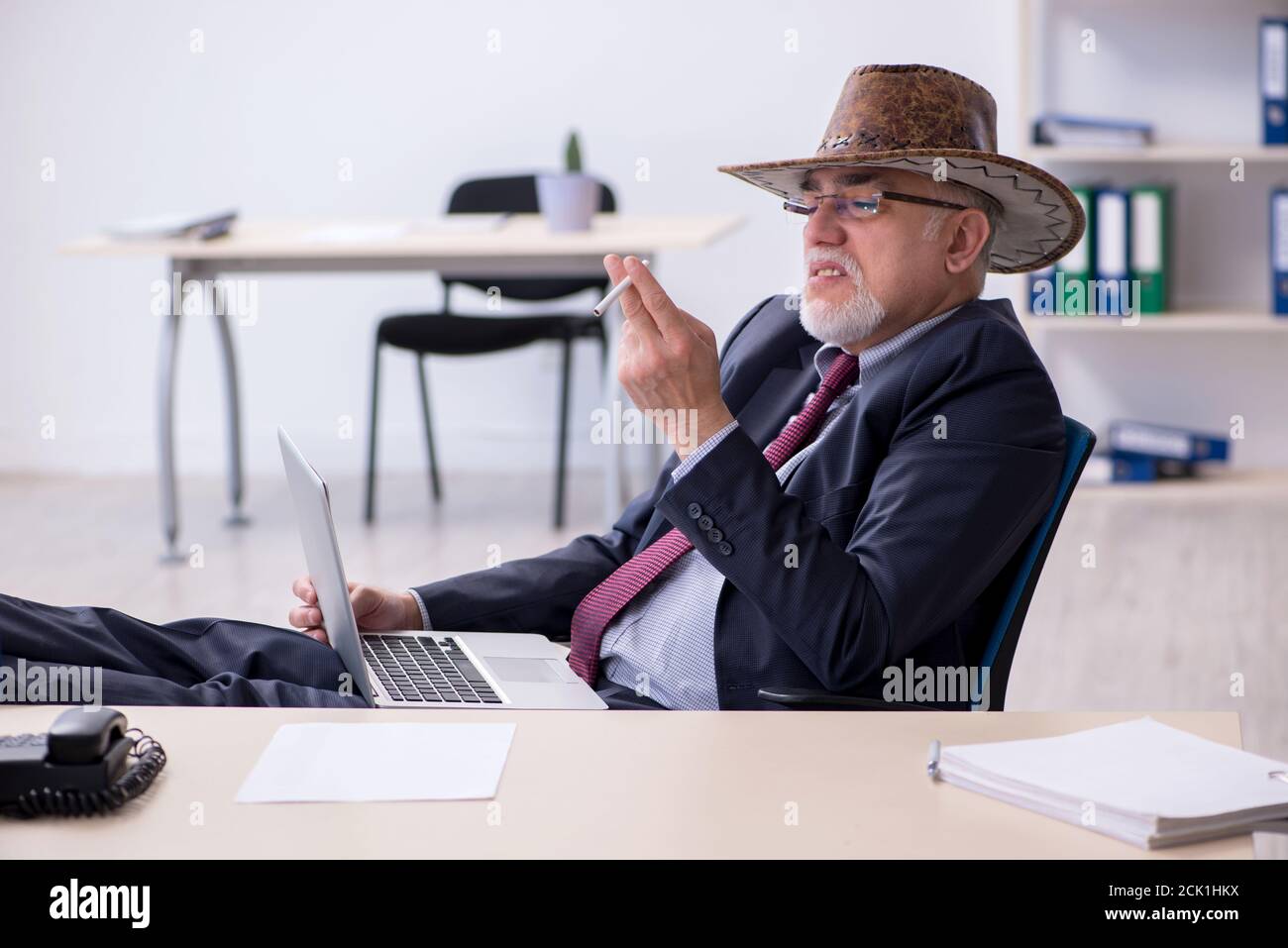 Funny old boss in cowboy hat in office Stock Photo - Alamy