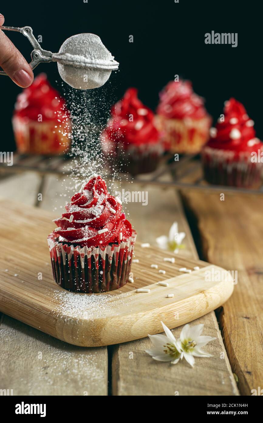 Vertical shot of a person adding sugar powder on a cupcake with red ...