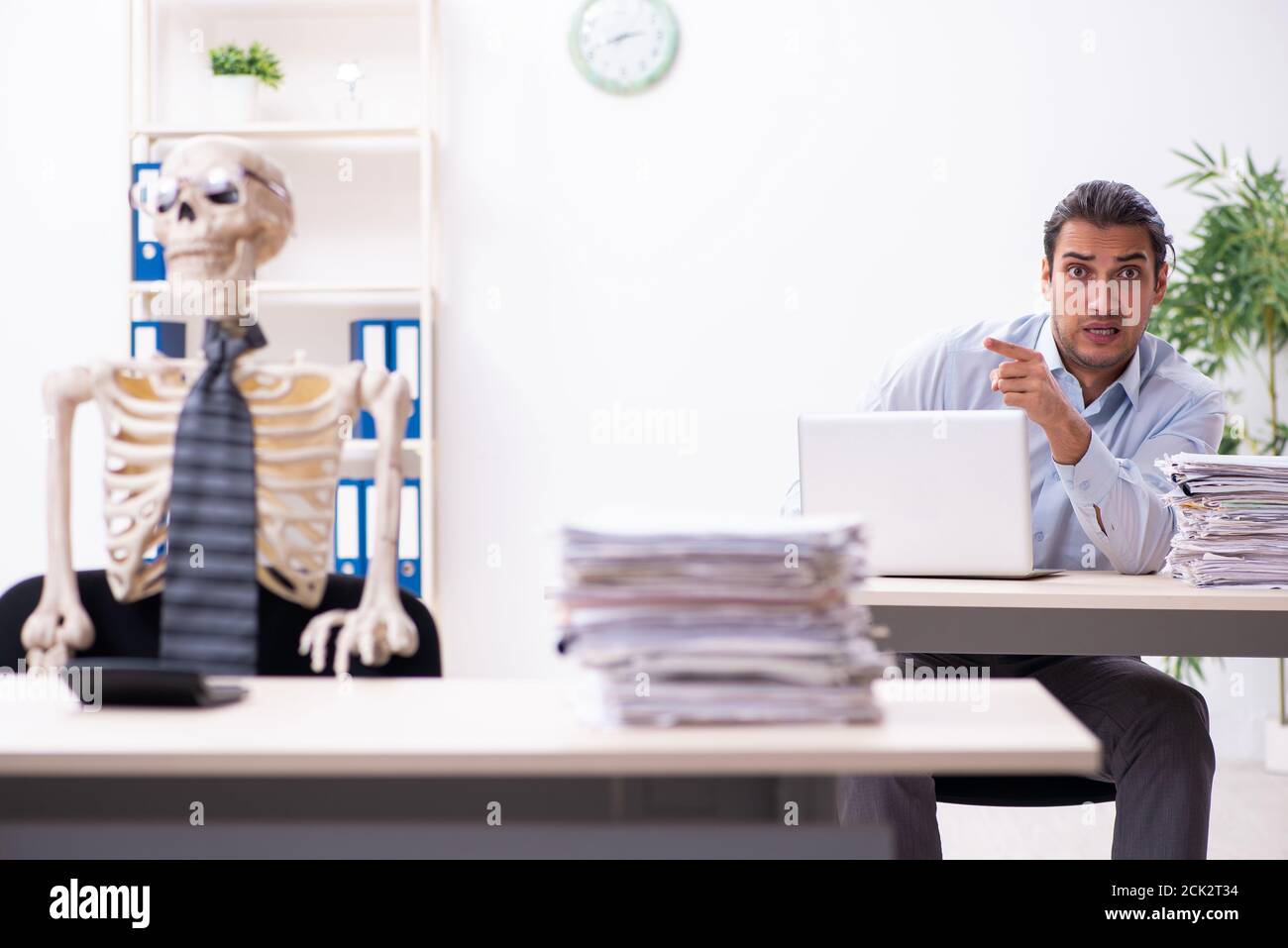 Young employee and skeleton in the office Stock Photo - Alamy