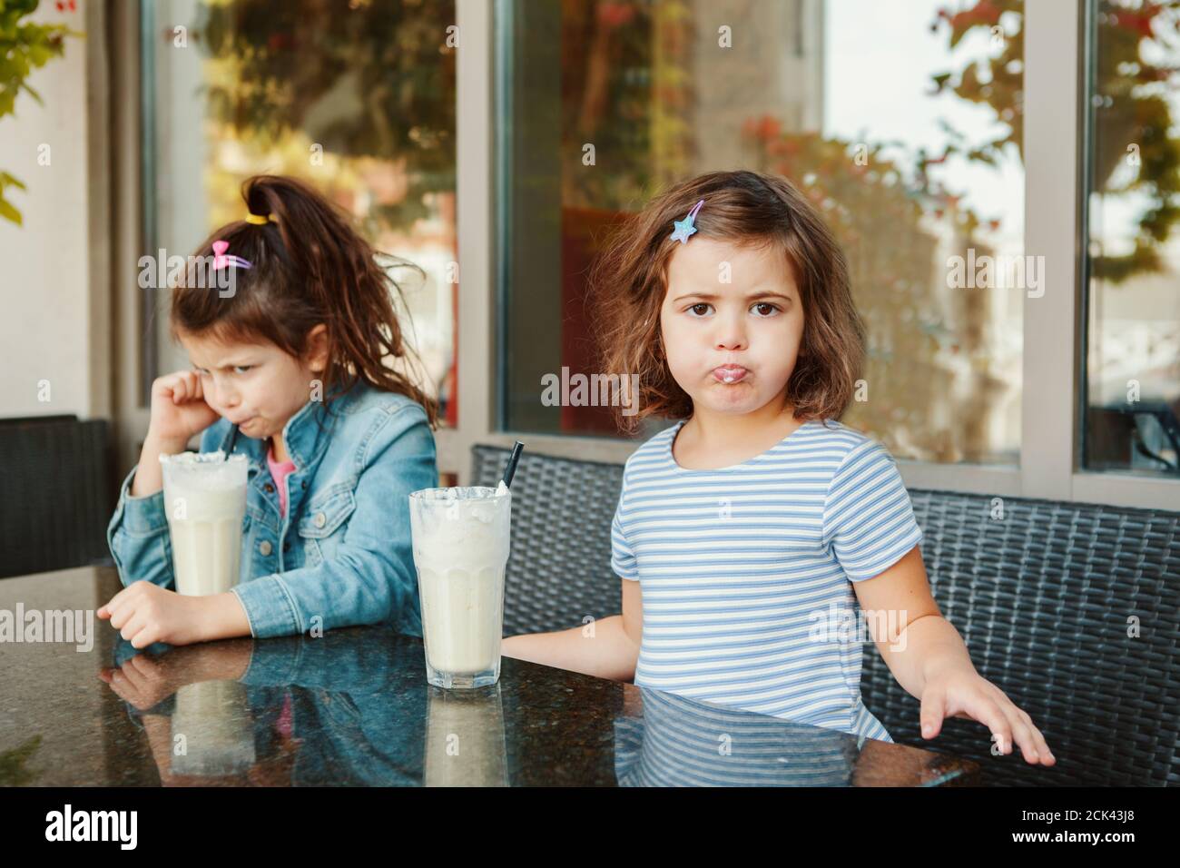 Two funny grumpy Caucasian little sisters siblings drink milk shakes in ...