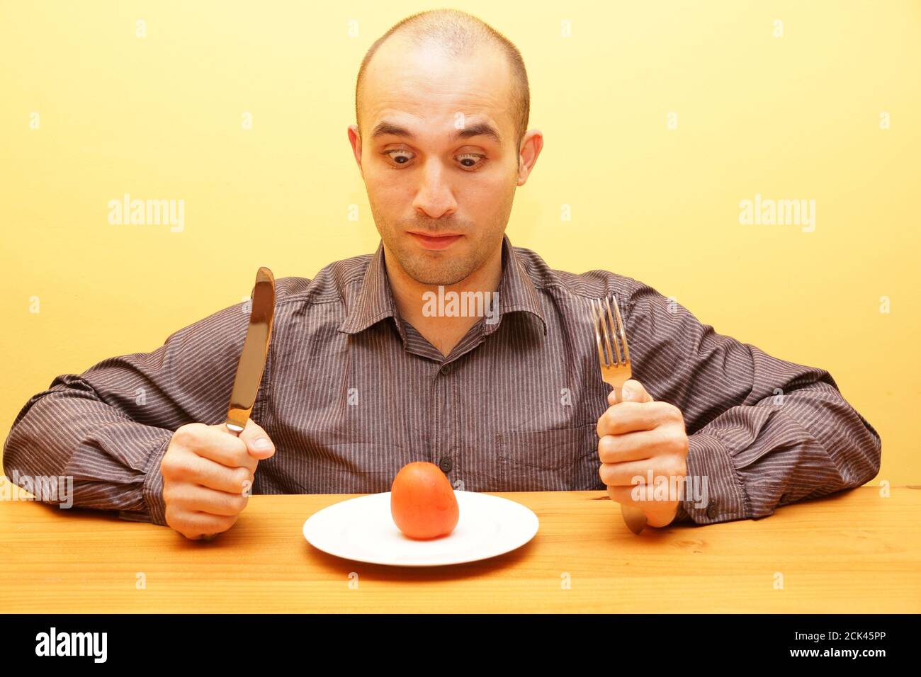 Closeup shot of a man holding knife and fork preparing to eat tomato ...