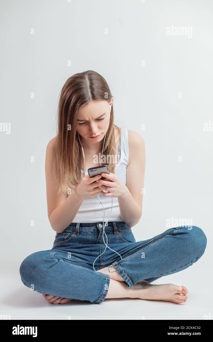 young woman is glaring at the cell phone. full length portrait ...
