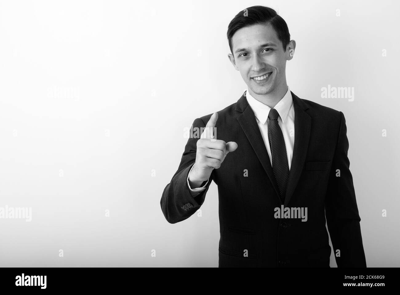 Studio shot of young happy businessman smiling while pointing finger ...