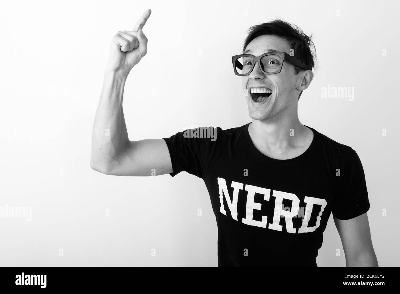 Studio shot of young happy nerd man smiling while thinking and pointing ...