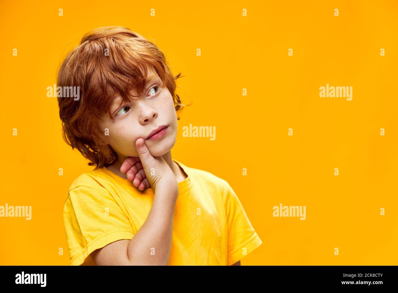Smart red-haired boy touches his face with his hand and looks to the ...