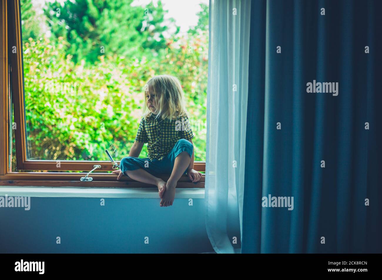 A little preschooler is sitting on a window sill in a bedroom Stock ...