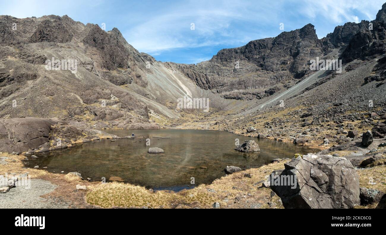 Lone female walker sits beside waters of Coire Lagan below the Cuillin ...