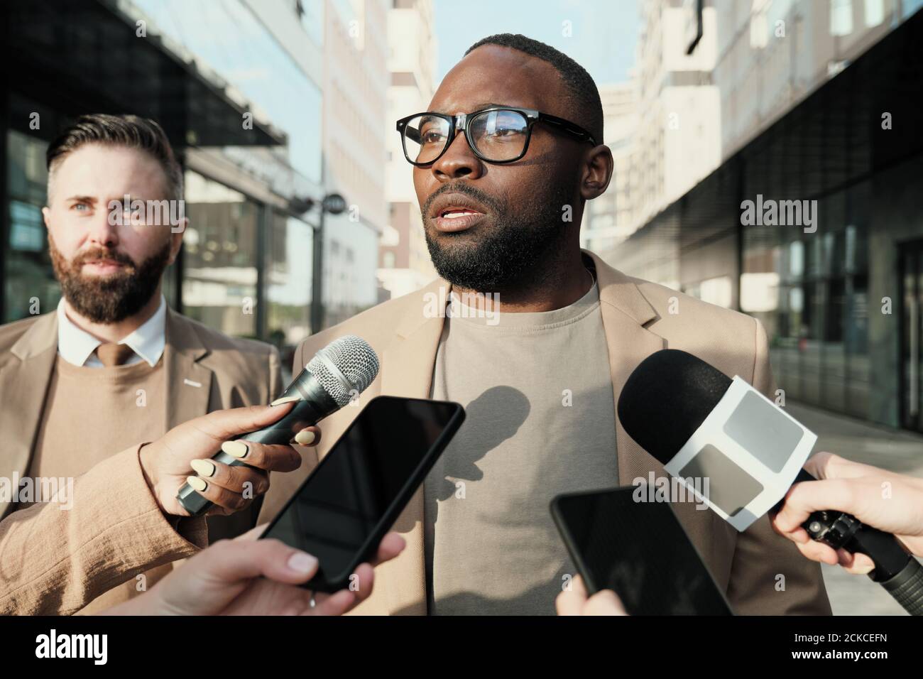 African man in eyeglasses standing in the city among journalists and ...