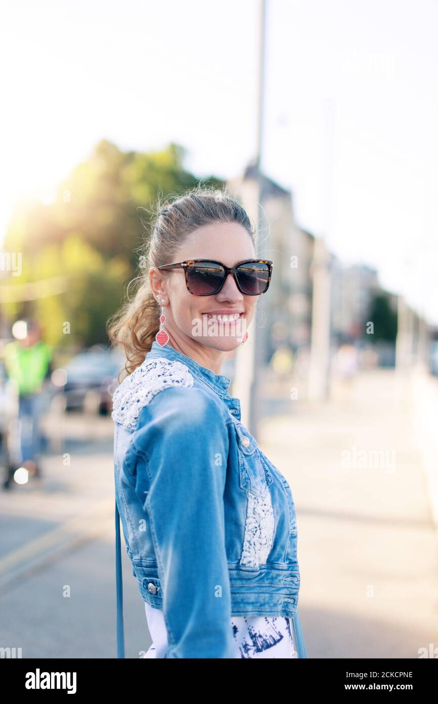 Happy young urban woman looking back on street with toothy smile Stock ...