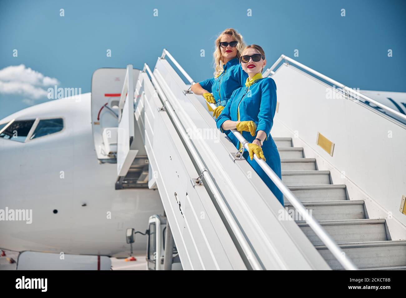 Two charming young women flight attendants in blue suits looking at ...