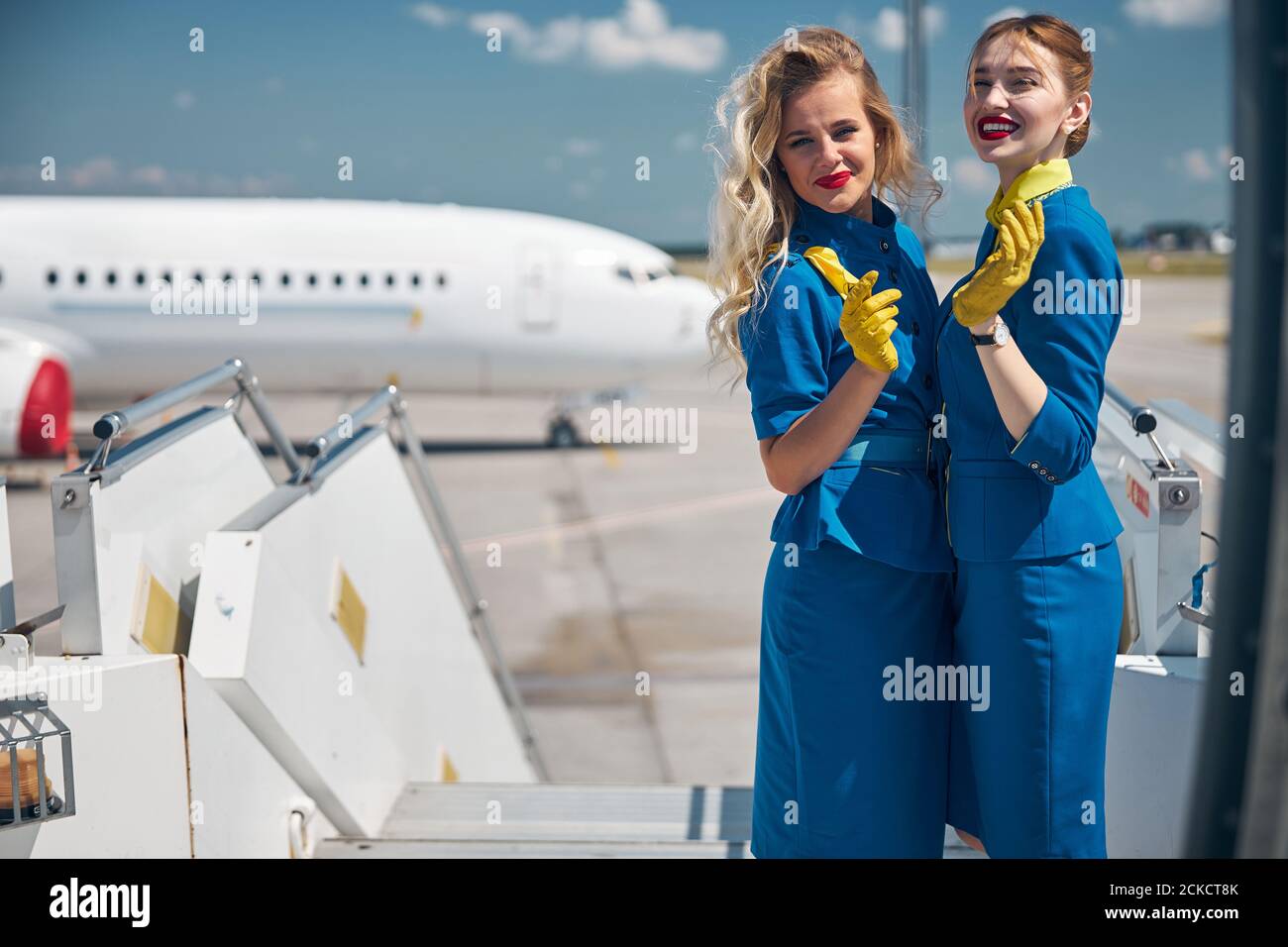 Two beautiful young women flight attendants in blue uniforms looking at ...