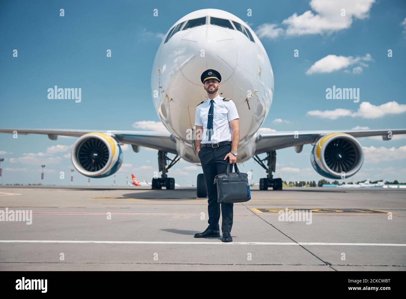 Handsome young man airline worker in captain hat holding travel bag and ...