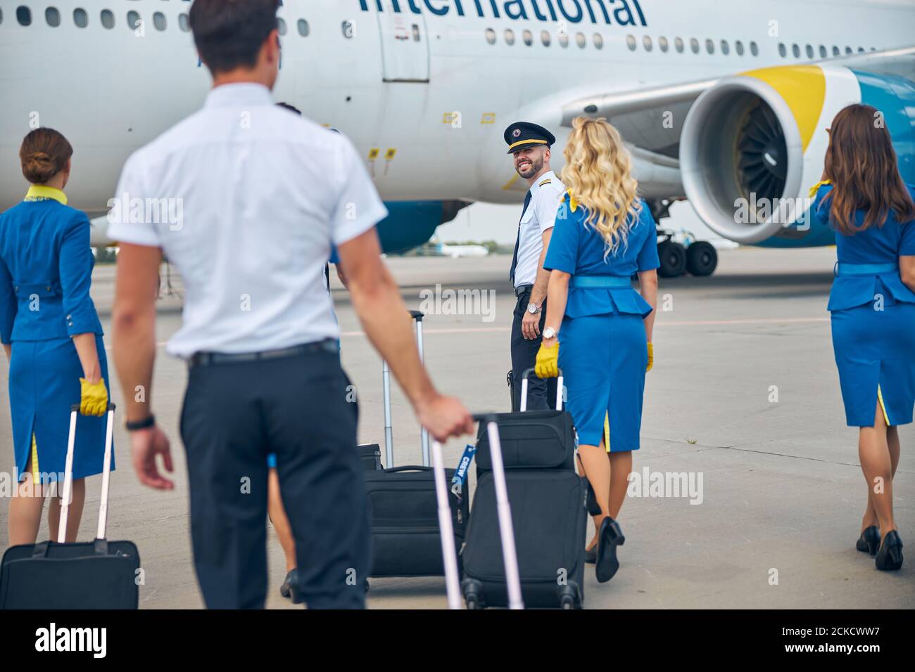Airline workers with travel bags walking down the airfield and heading ...