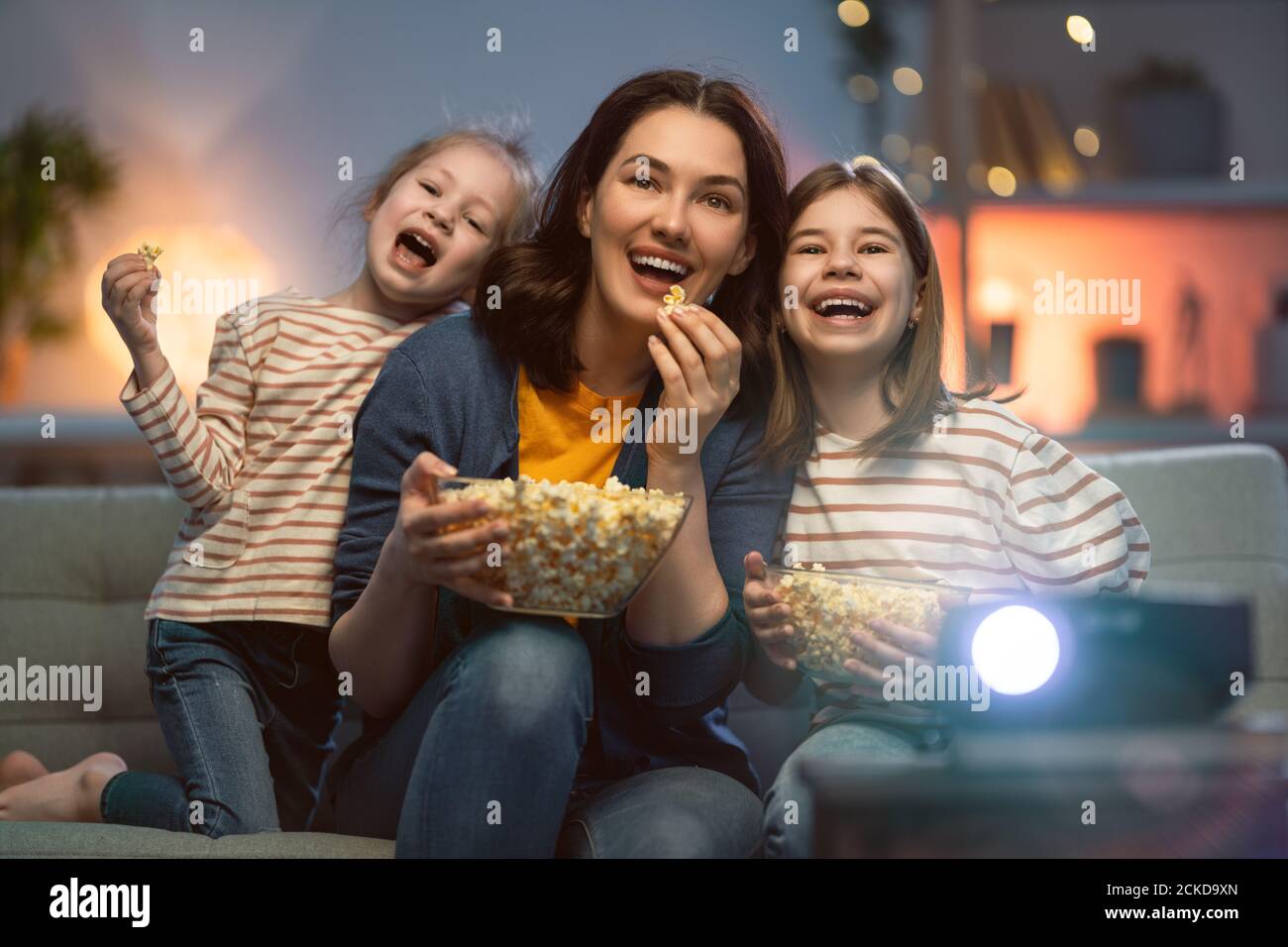 Happy family watching projector, TV, movies with popcorn in the evening ...