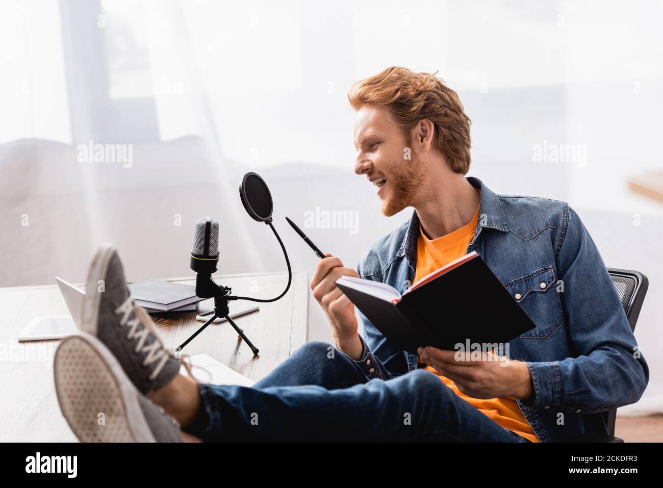 excited announcer holding notebook and pen while sitting with legs on ...