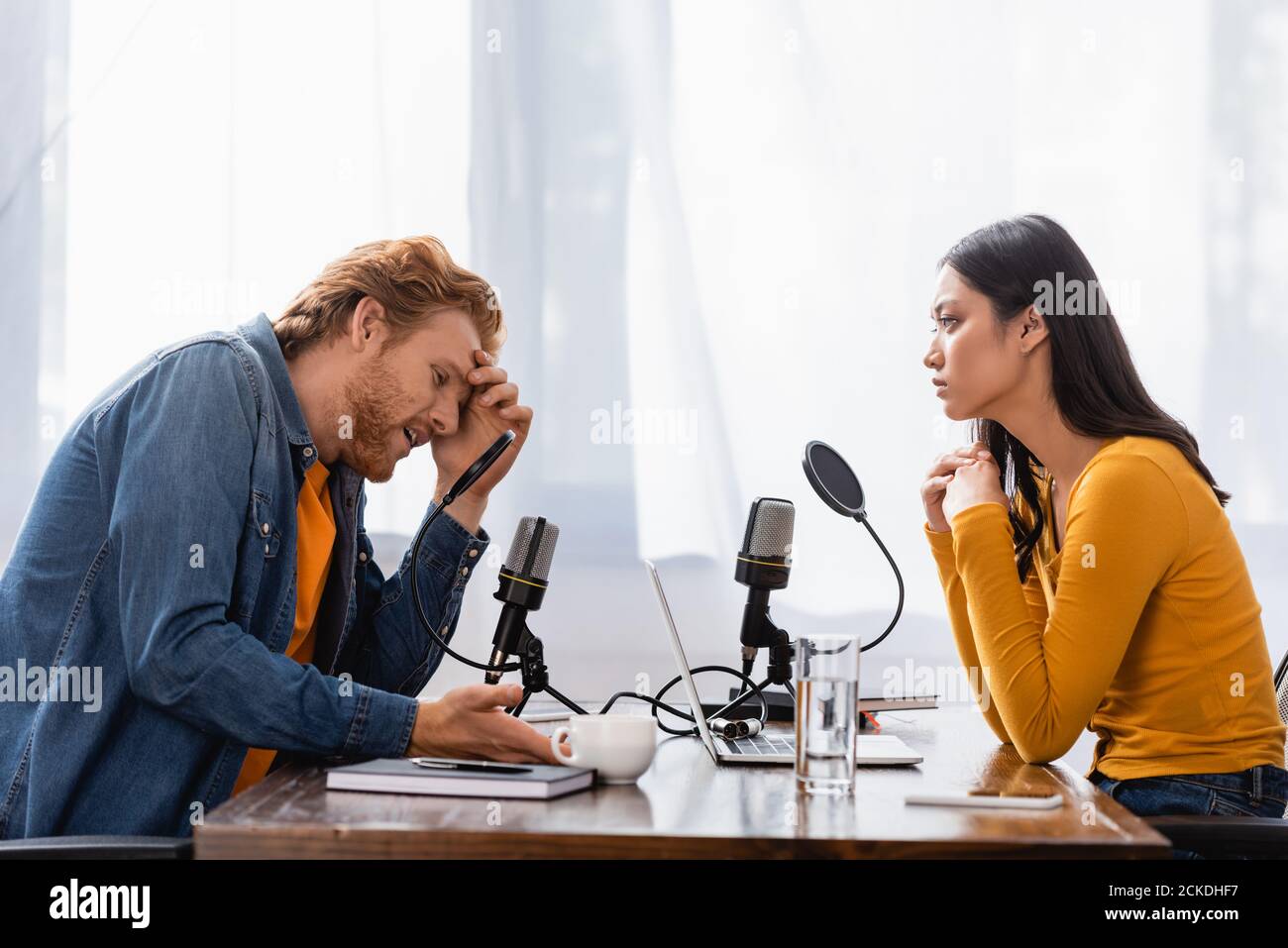 young asian radio host looking at tense man touching head during ...
