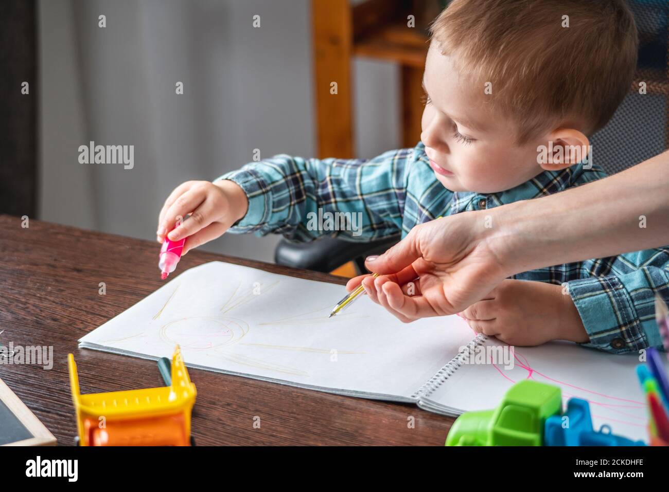Mom is helping cute child to draw with pencils on paper in an album at ...