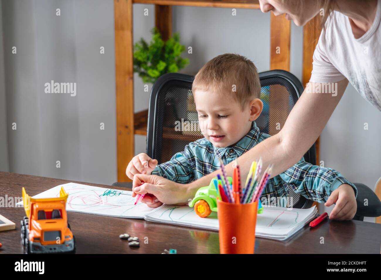 Mom is helping cute child to draw with pencils on paper in an album at ...