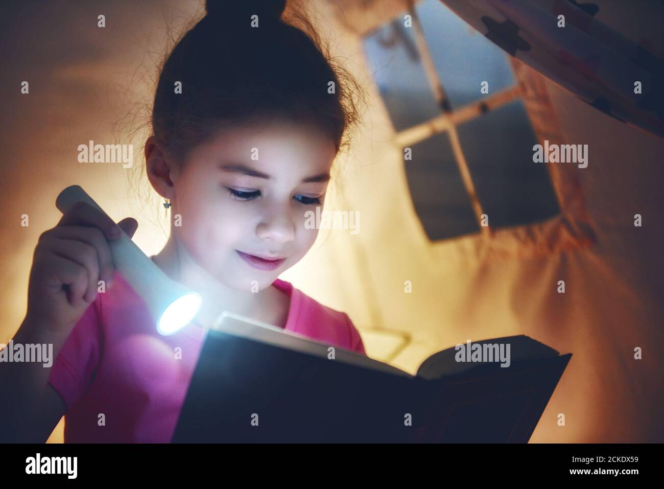 Cute little child is reading a book with flashlights in tent. Happy ...