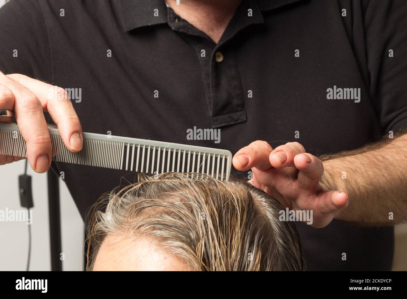 Professional hairdresser cutting a woman's hair with scissors and a ...