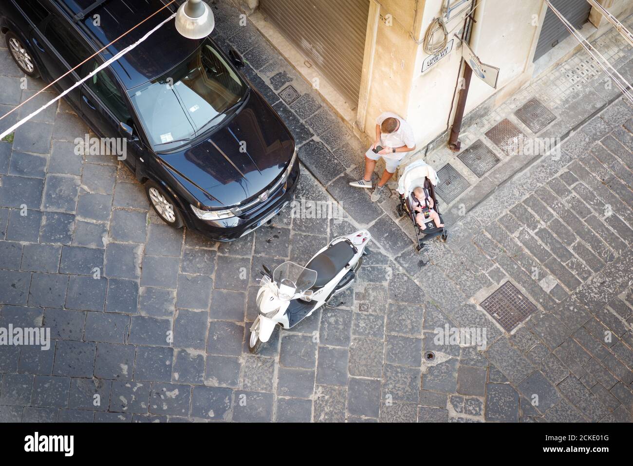 Dad with a baby in a stroller waiting at a street corner in Noto ...