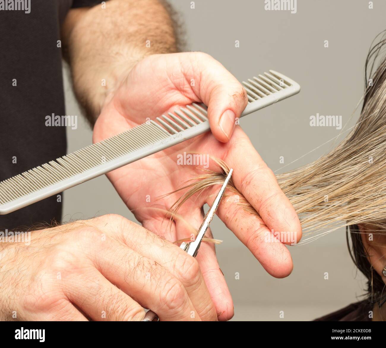 Professional hairdresser cutting a woman's hair with scissors and a ...